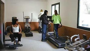 Uma academia com equipamentos de ginástica, incluindo esteira, bicicletas ergométricas e aparelhos de musculação.