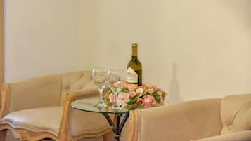 Uma mesa de vidro com uma garrafa de vinho, duas taças de vinho e um buquê de flores sobre um sofá bege.