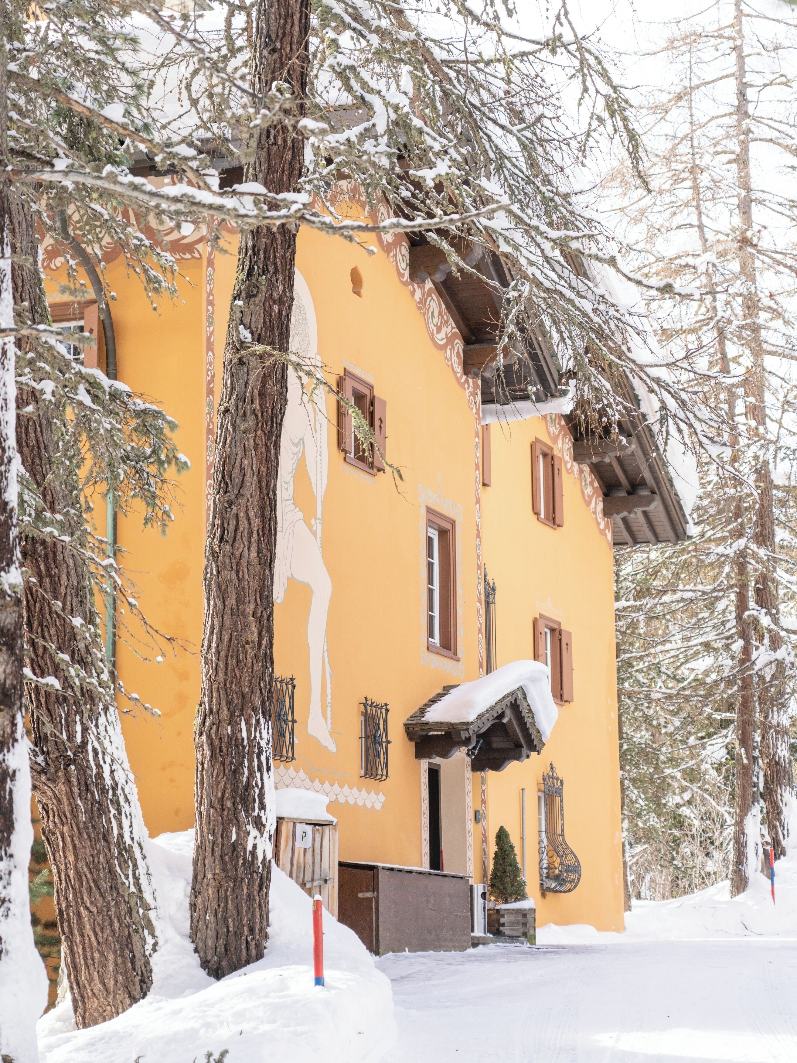 Um edifício coberto de neve com fachada amarela, janelas amplas e porta com pequena varanda.