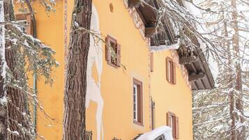 Um edifício coberto de neve com fachada amarela, janelas amplas e porta com pequena varanda.