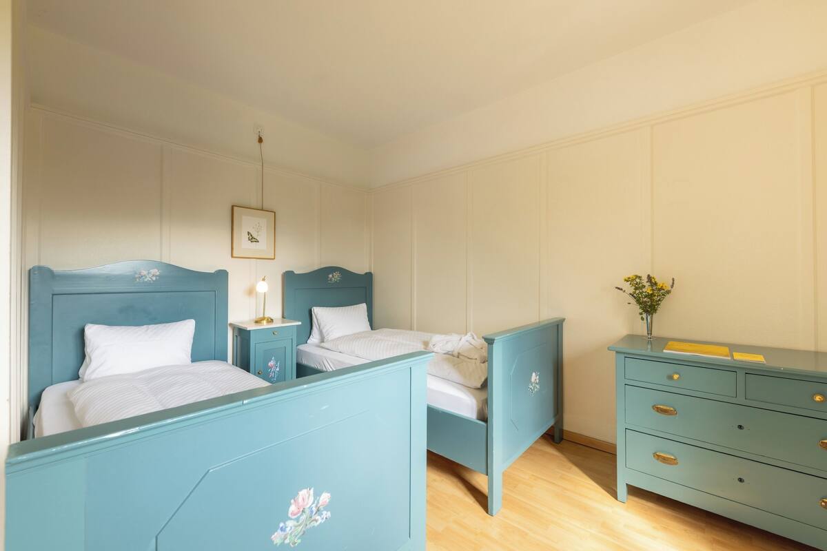 Quarto com duas camas, uma cômoda e mesa de cabeceira com abajur.