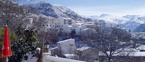 Uma aldeia montanhosa coberta de neve, com edifícios e um guarda-chuva vermelho em primeiro plano.