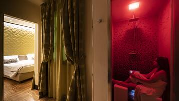 Quarto com cama, poltrona de massagem e área iluminada em vermelho.