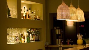 Uma área de bar com prateleiras cheias de garrafas de bebidas e copos, uma geladeira e luminárias pendentes de vime.