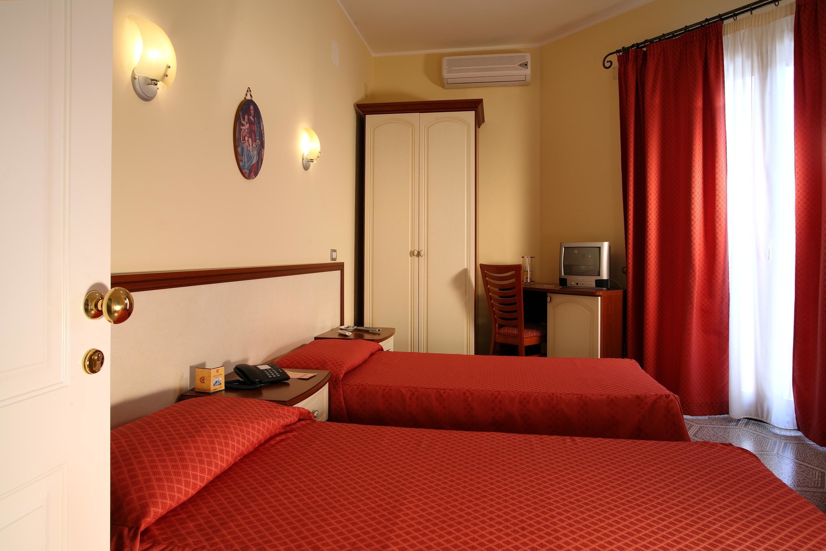 Quarto de hotel com duas camas, uma escrivaninha com cadeira, televisão e guarda-roupa.