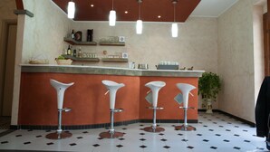 Uma área de bar com três banquetas brancas, um balcão com prateleiras e luminárias pendentes.