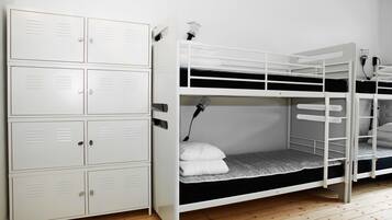 Uma cama beliche com estrutura metálica branca, um conjunto de armários brancos e piso de madeira.