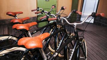 Uma fileira de bicicletas com assentos laranja e estrutura preta, estacionadas em um espaço interno com piso de madeira e uma porta verde ao fundo.
