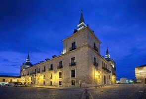 Um edifício histórico com uma torre imponente e duas torres pontiagudas, apresentando um pátio e um chão de pedras.