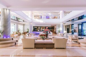Um lobby espaçoso com área de estar central, balcão de recepção e vista para o andar superior.