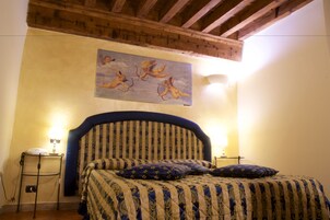 Quarto com cama, mesa de cabeceira, abajur e um quadro na parede.