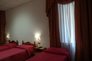 Quarto de hotel com duas camas de solteiro, cabeceiras de madeira e mesa de cabeceira com luminária.