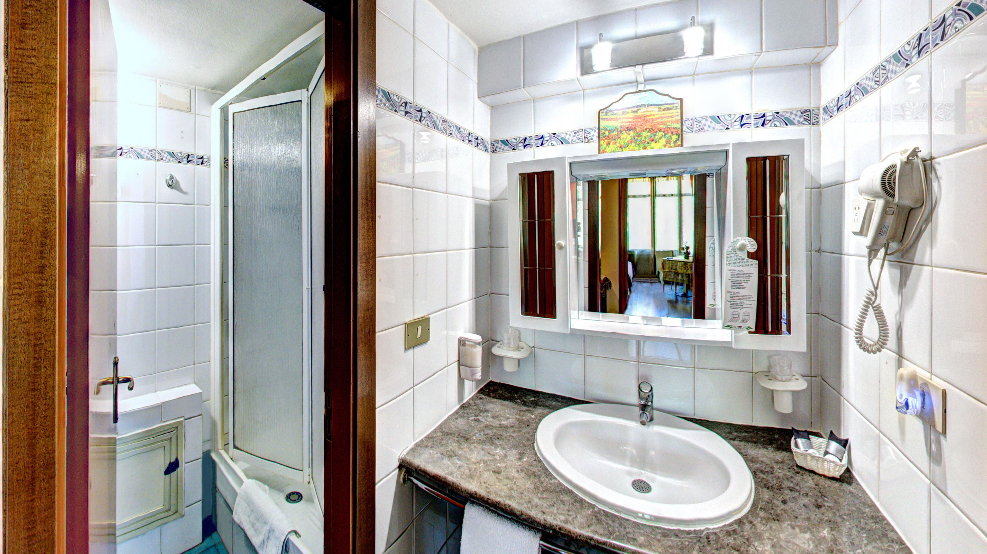 Casa de banho com lavatório, espelho e secador de cabelo fixado na parede.