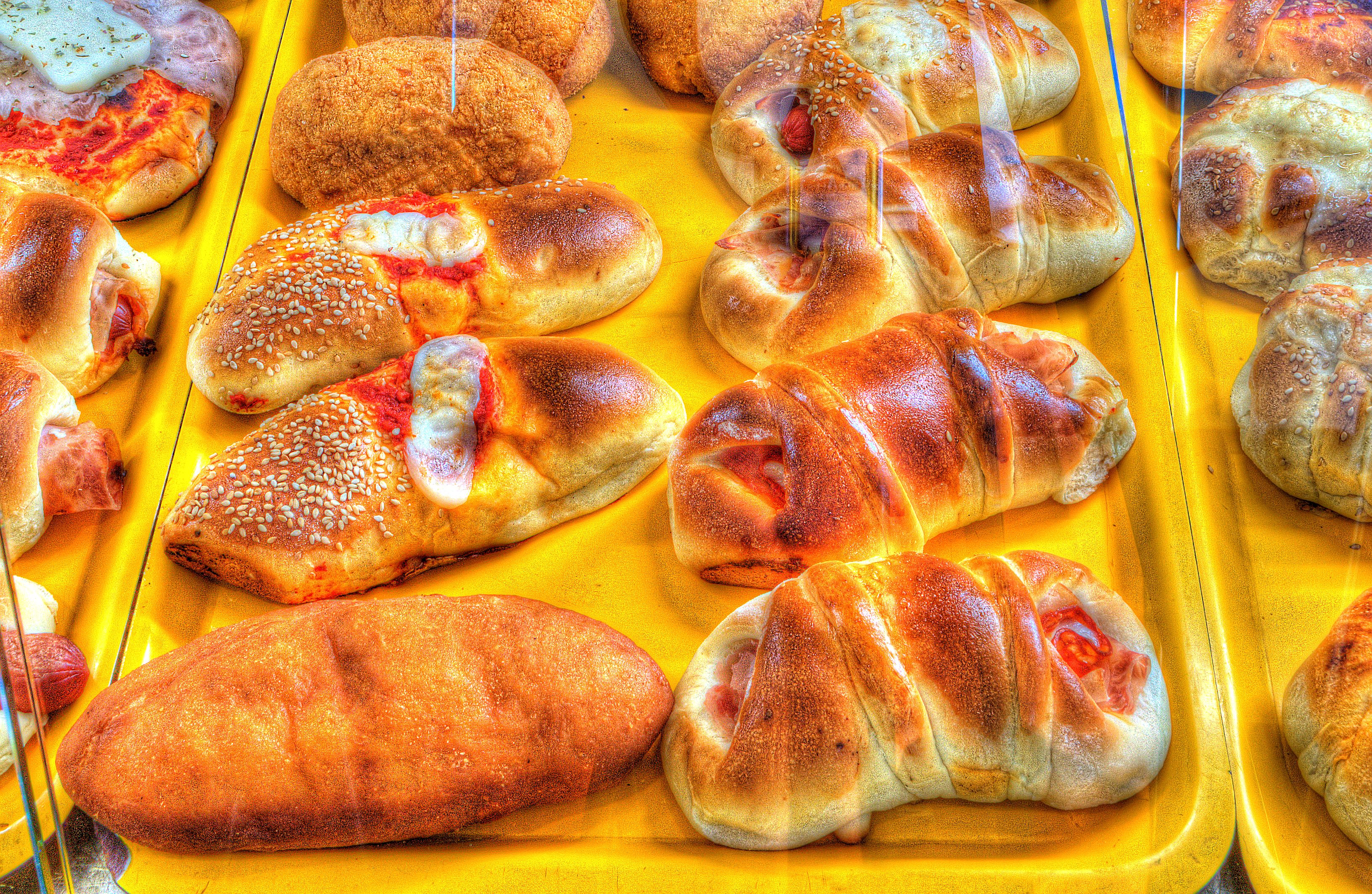 Diversos produtos de panificação expostos numa bandeja amarela.