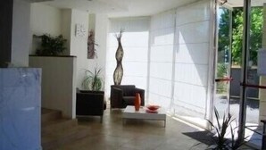 Uma sala espaçosa com uma grande porta de vidro deslizante que dá para uma varanda, um sofá, uma mesa de centro e um vaso decorativo.
