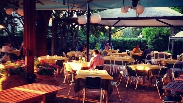 Restaurante ao ar livre com mesas e cadeiras sob uma área coberta, rodeado por vegetação.