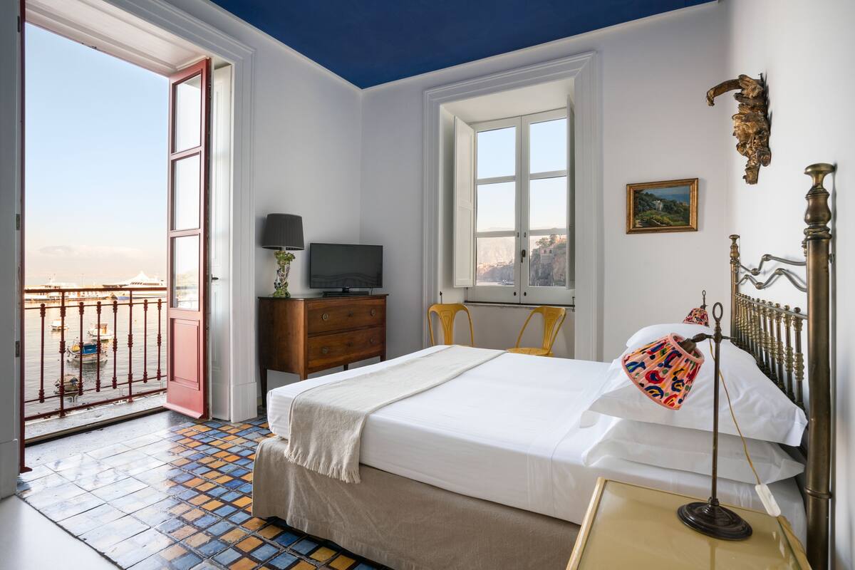 Quarto com cama, penteadeira, televisão e janela com vista.