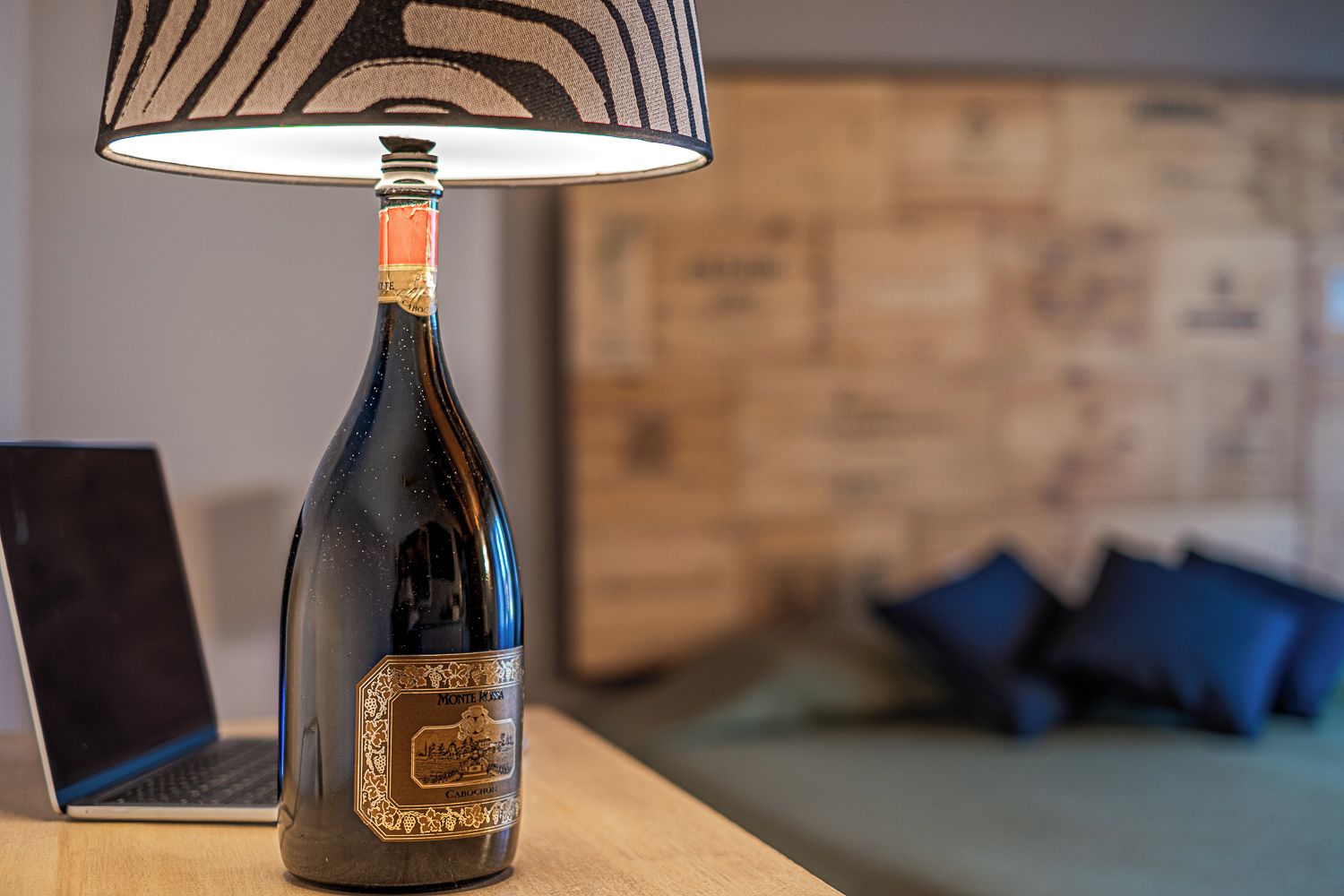 Uma garrafa de vinho Monte Ruso com etiqueta, colocada sobre uma superfície de madeira sob um candeeiro com cúpula estampada.