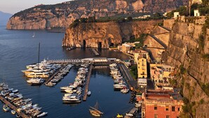 Uma marina costeira com barcos atracados, um rochedo e edifícios ao longo da orla.
