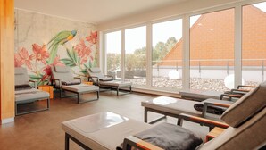 Um quarto com várias poltronas, uma janela grande com vista para um edifício de tijolos e um mural de flores e um pássaro na parede.