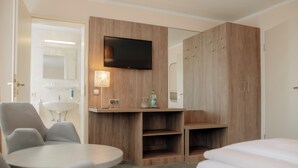 Quarto de hotel com televisão fixada numa parede de madeira, secretária com candeeiro, cadeira, cama e guarda-roupa.