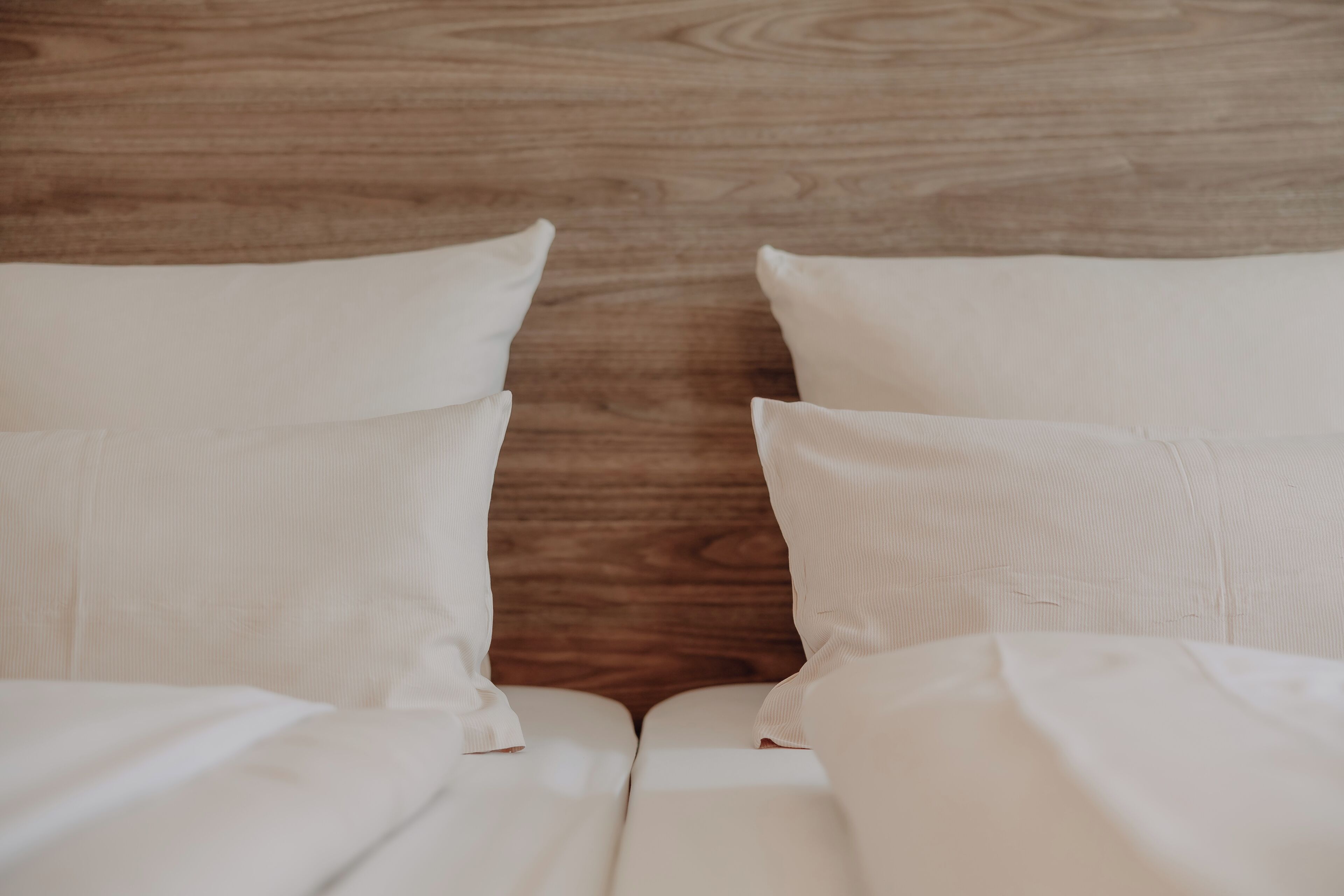 Cama com roupa de cama e almofadas brancas encostadas a uma cabeceira de madeira.