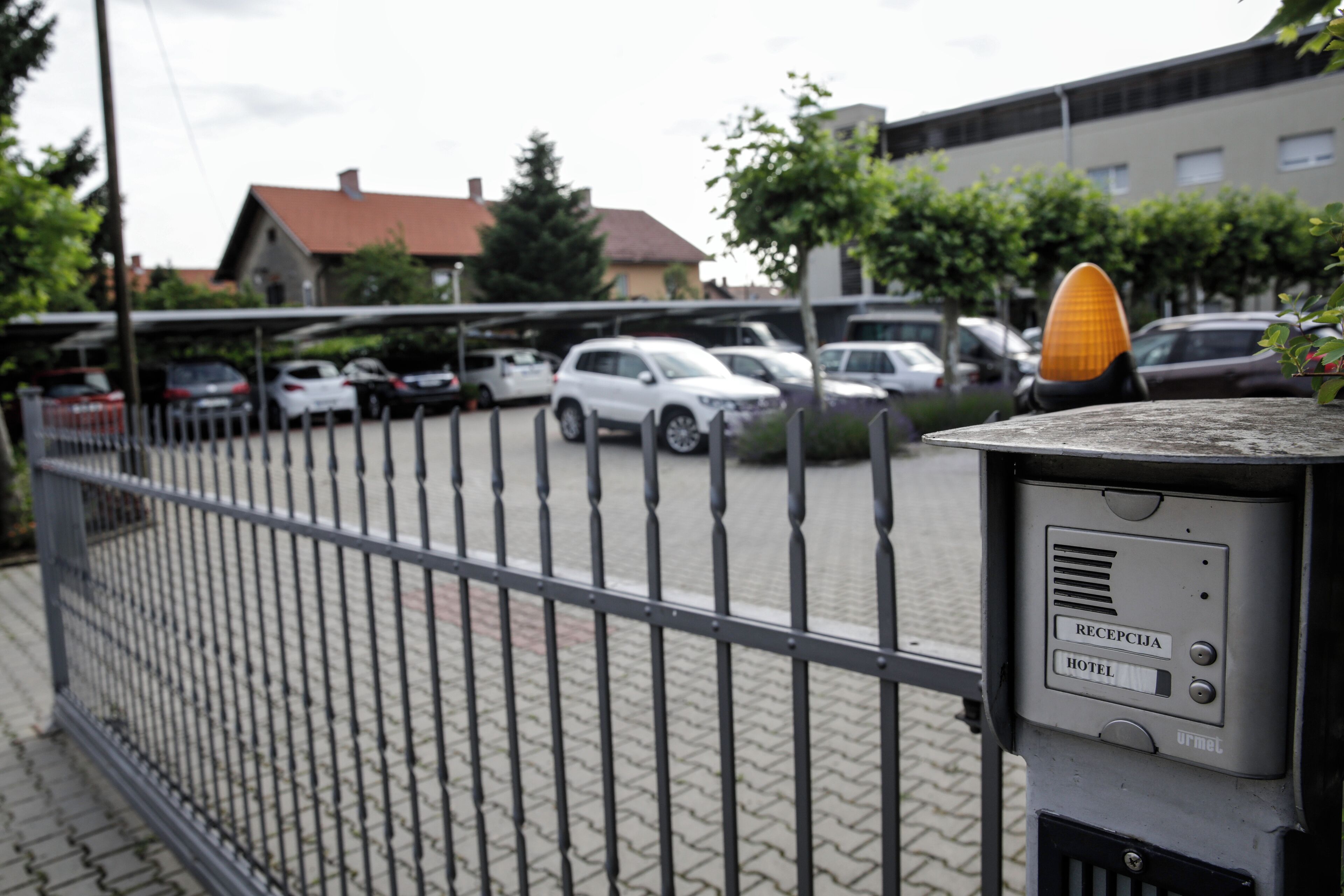 Uma área de estacionamento com cerca de metal, uma área de recepção e vários carros estacionados.