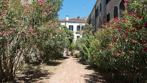 Um caminho de paralelepípedos estreito ladeado por vegetação exuberante e edifícios com janelas em arco.