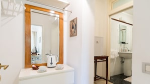 Casa de banho de hotel com lavatório, espelho e uma pequena mesa com uma chaleira e chávenas.