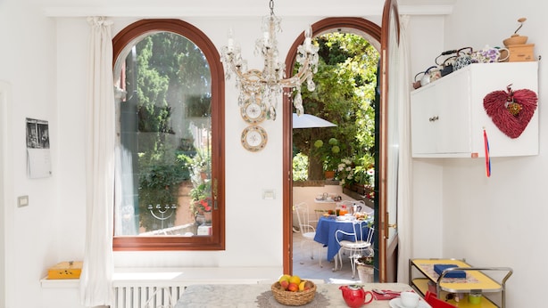Um quarto com uma mesa de jantar posta para o café da manhã, um candelabro e vista para um jardim através de grandes janelas.