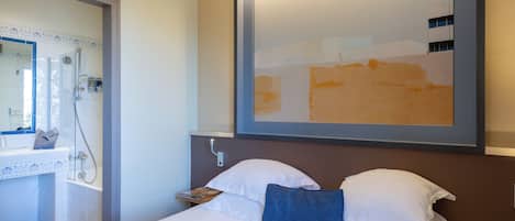 Quarto de hotel com cama, mesa de cabeceira, espelho e área de chuveiro.