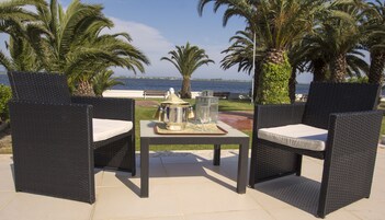 Área de estar externa com cadeiras de vime e uma mesa, com vista para um corpo de água.