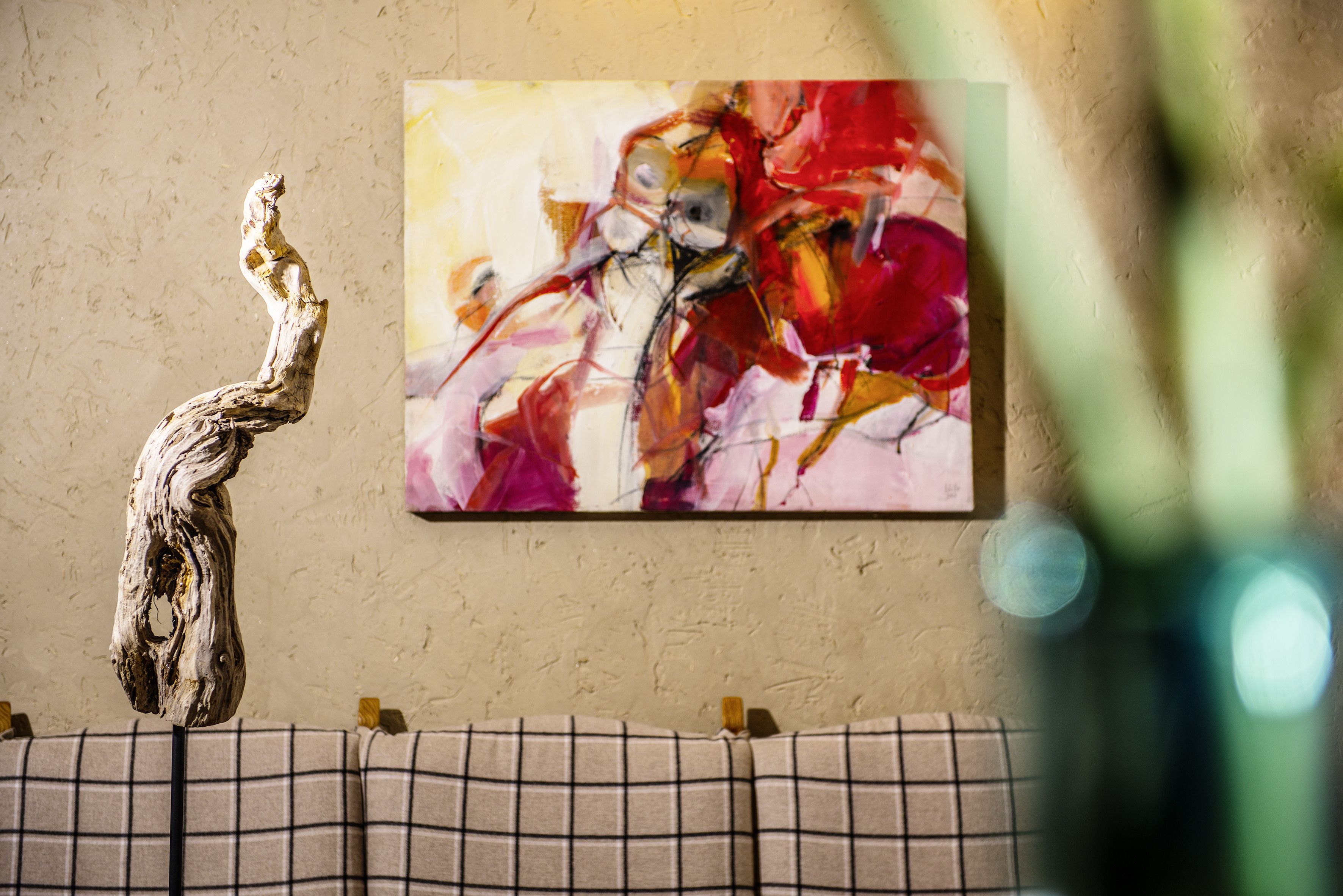 Quarto com uma escultura de madeira em um suporte, um quadro na parede e um sofá xadrez.
