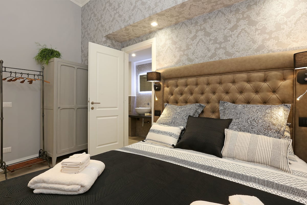 Quarto com uma cama grande, um guarda-roupa e um banheiro visível ao fundo.
