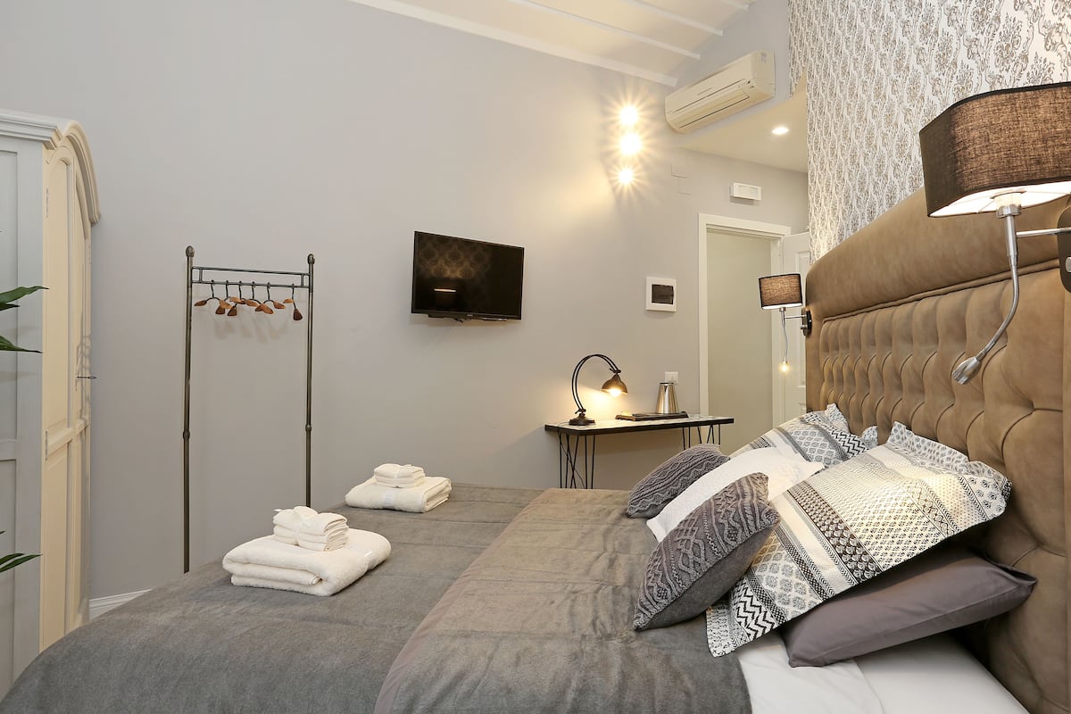 Quarto com cama, televisão, escrivaninha e espelho.