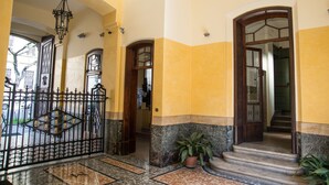 Um corredor com paredes amarelas, piso de mármore e portão de ferro forjado.