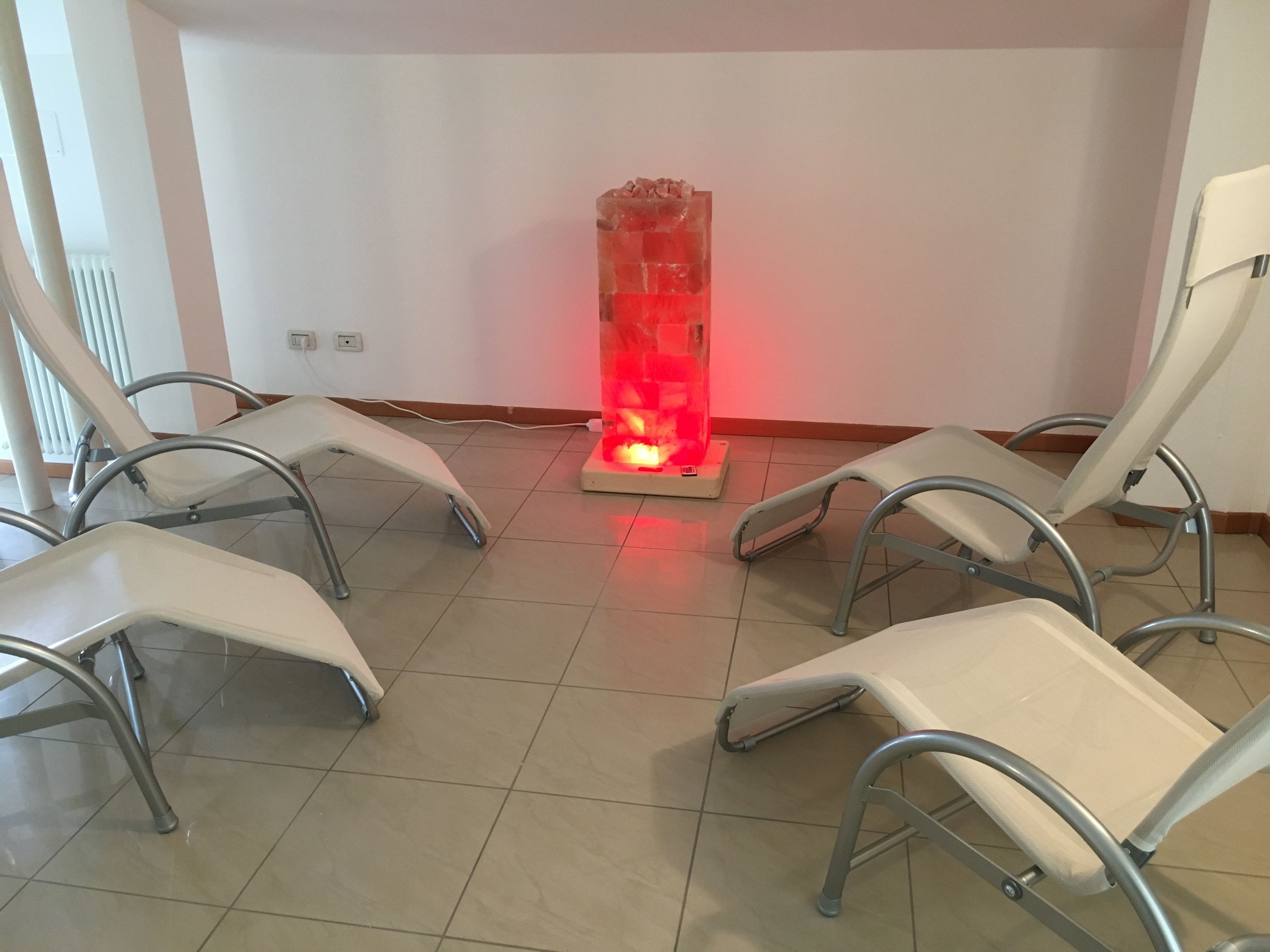 Uma área de espera com quatro cadeiras de estrutura metálica dispostas em semicírculo ao redor de uma fonte central iluminada em vermelho.
