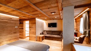 Interior de uma cabana de madeira com uma cama, um sofá, uma TV fixada na parede e uma mesa pequena.