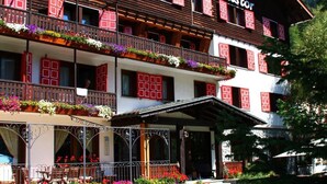 Um hotel com arquitetura alpina tradicional, com varandas adornadas com caixas de flores e um jardim bem cuidado.