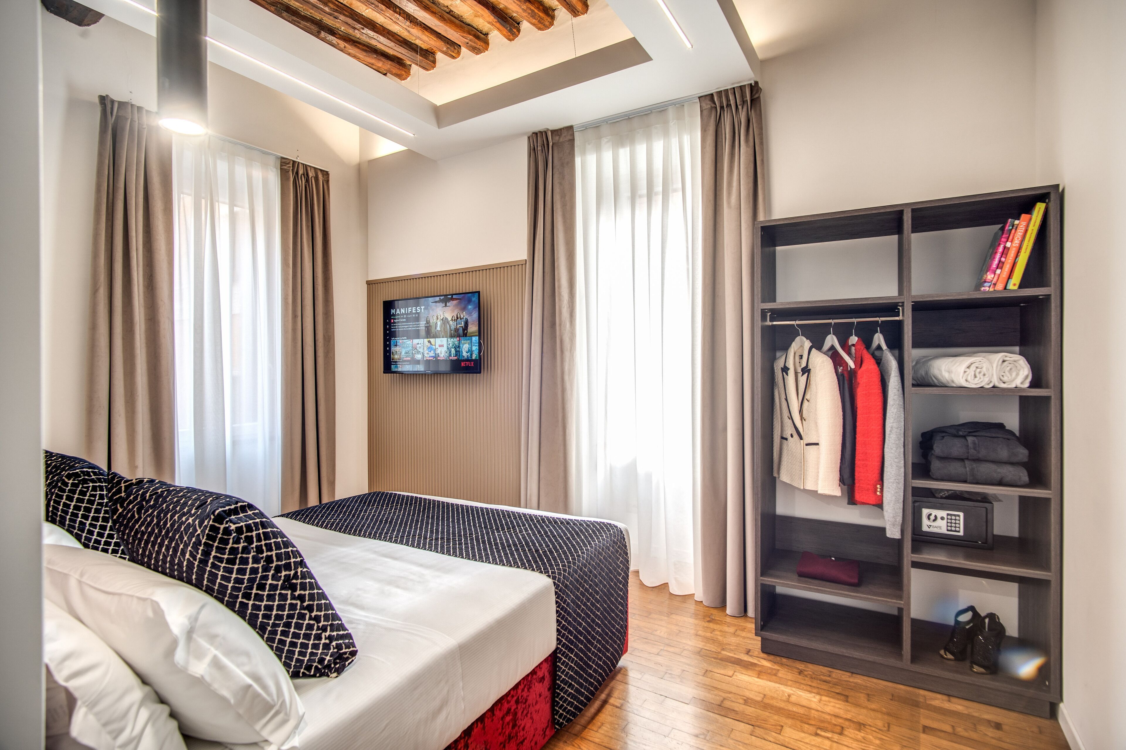 Quarto de hotel com cama, televisão, guarda-roupa e chão de madeira.