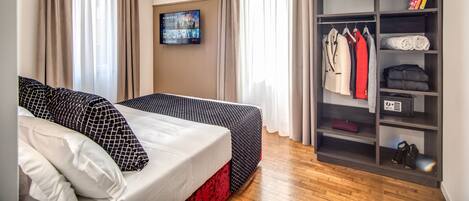 Quarto de hotel com cama, televisão, guarda-roupa e chão de madeira.