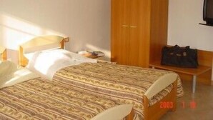 Quarto de hotel com cama, guarda-roupa, escrivaninha e televisão.
