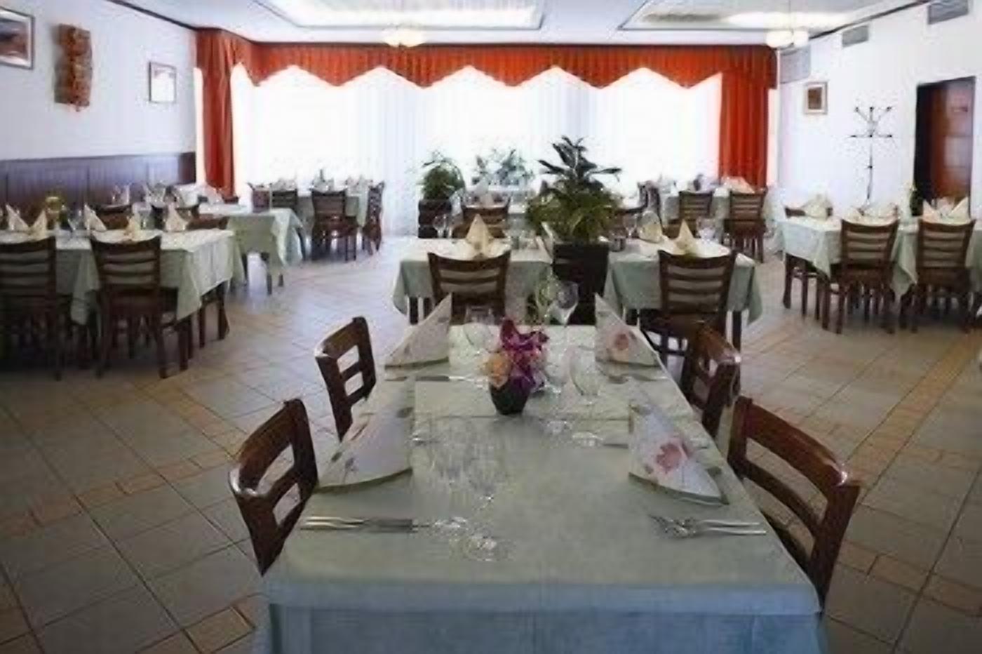 Uma sala de jantar com várias mesas preparadas para o serviço, cadeiras e um arranjo floral central.