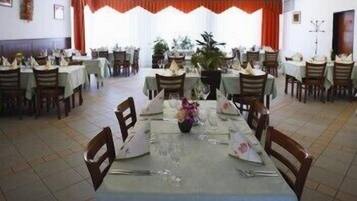 Uma sala de jantar com várias mesas preparadas para o serviço, cadeiras e um arranjo floral central.