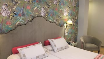 Quarto de hotel com cama, duas almofadas, mesa de cabeceira, abajur e uma cadeira.
