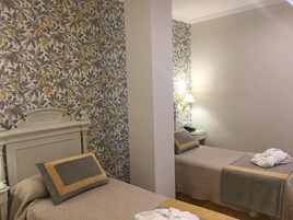 Quarto de hotel com duas camas, papel de parede floral, uma mesa de cabeceira com abajur e um espelho.