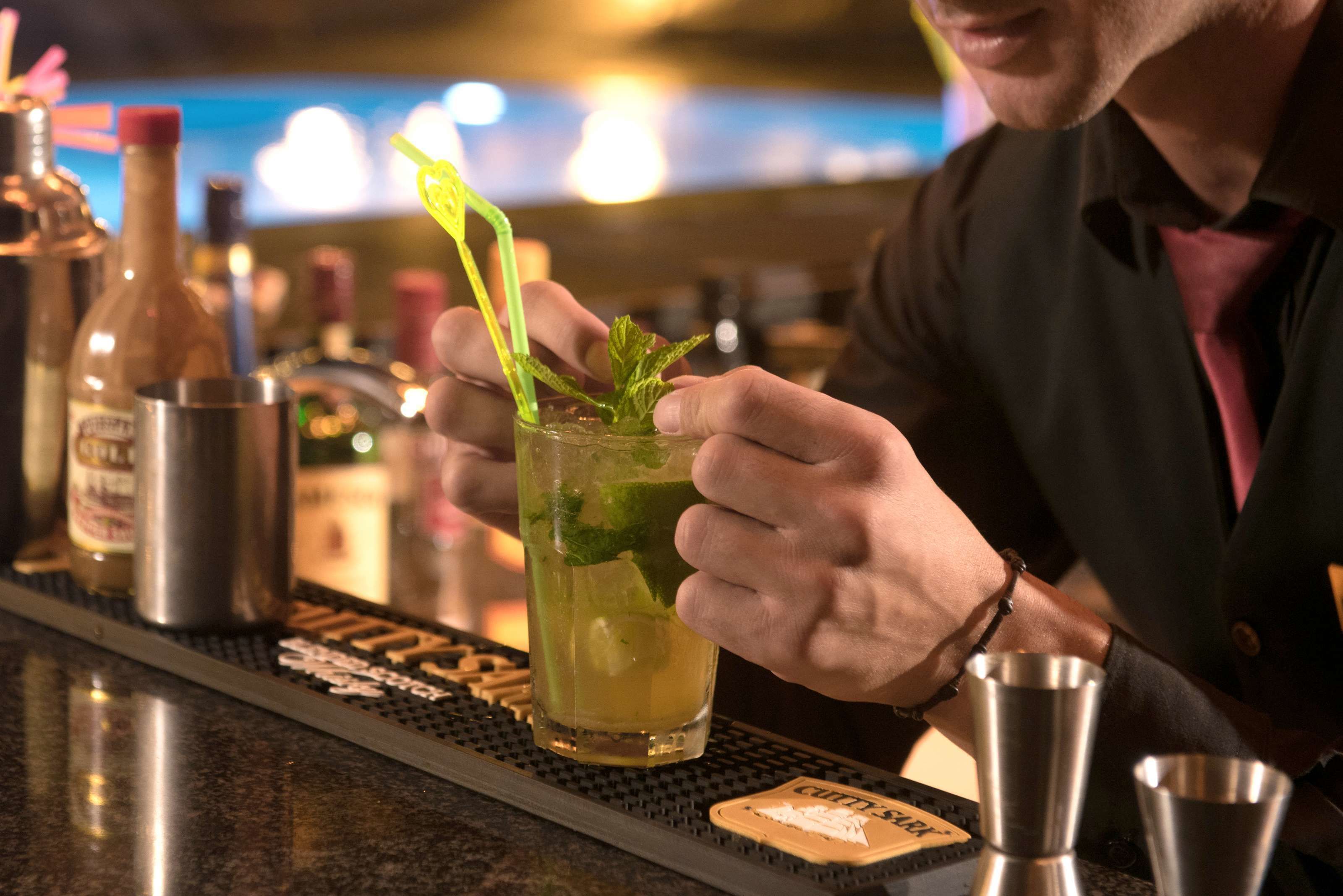 Um bartender preparando um cocktail com enfeite de limão e hortelã.