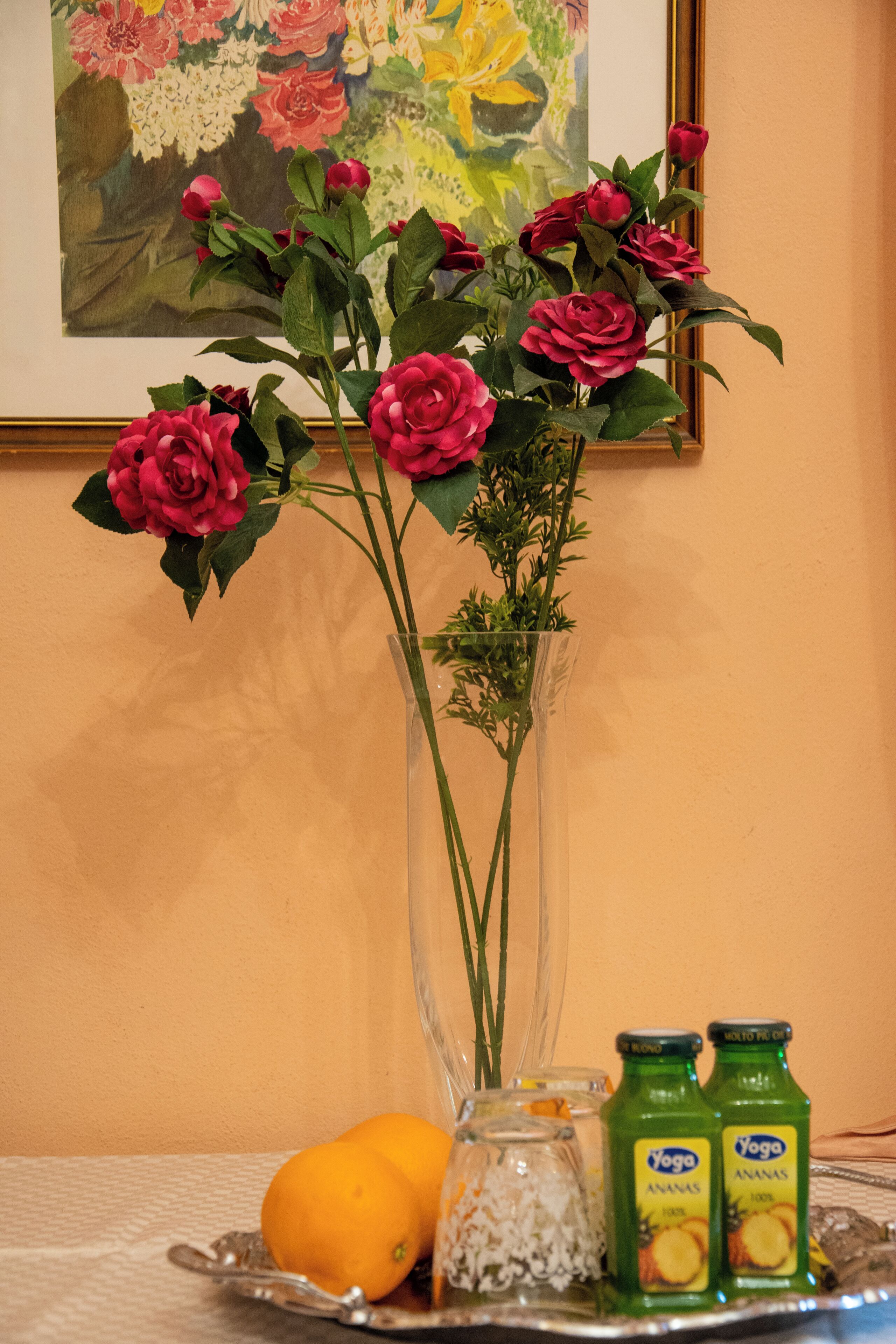 Um vaso com flores cor-de-rosa, um pote de vidro e duas garrafas de 'Yoga Avanas' sobre um suporte.