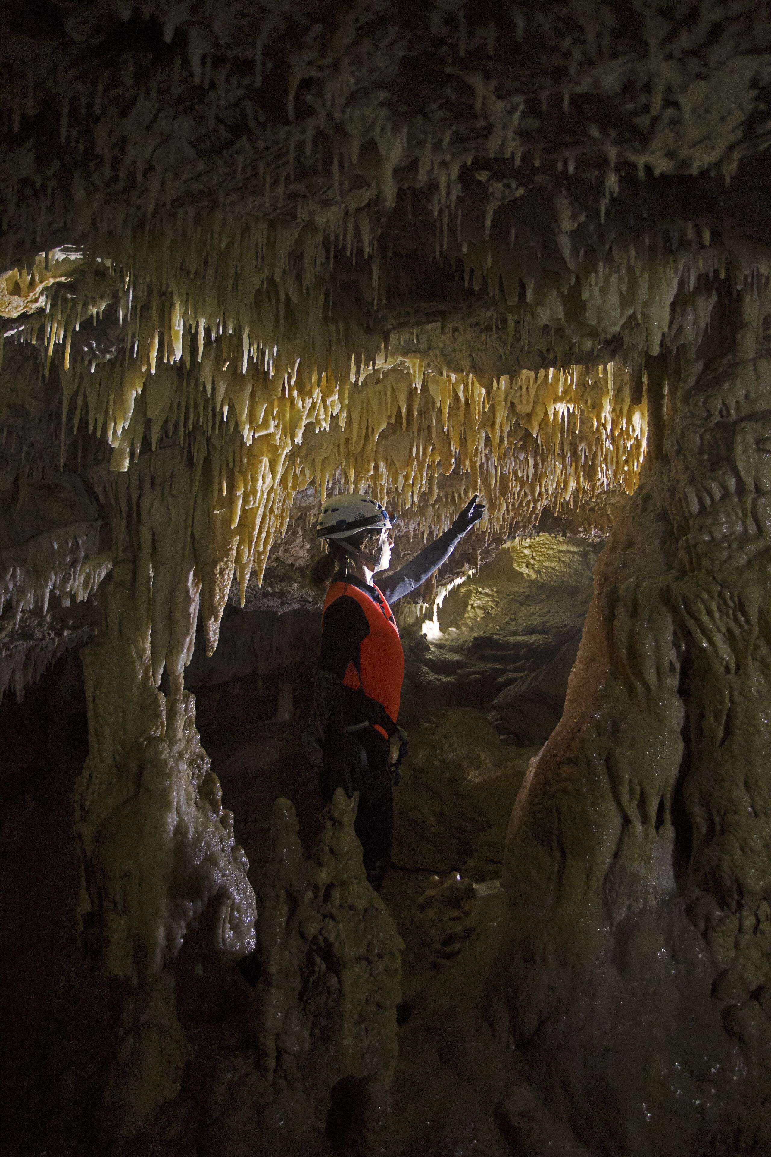 Uma pessoa dentro de uma caverna, com estalactites e estalagmites, usando capacete e equipamentos de segurança.