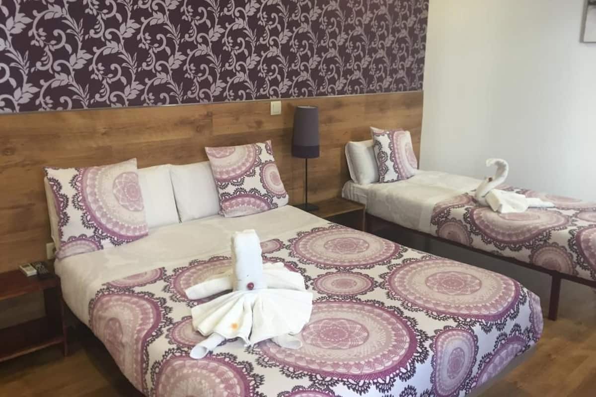 Quarto de hotel com duas camas, cada uma com colcha estampada e almofadas combinando. Há uma cabeceira de madeira, uma mesinha de cabeceira e um abajur.